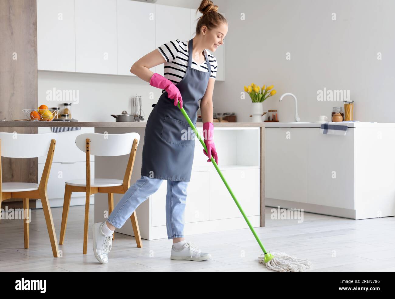 Pretty young woman mopping floor in light kitchen Stock Photo - Alamy