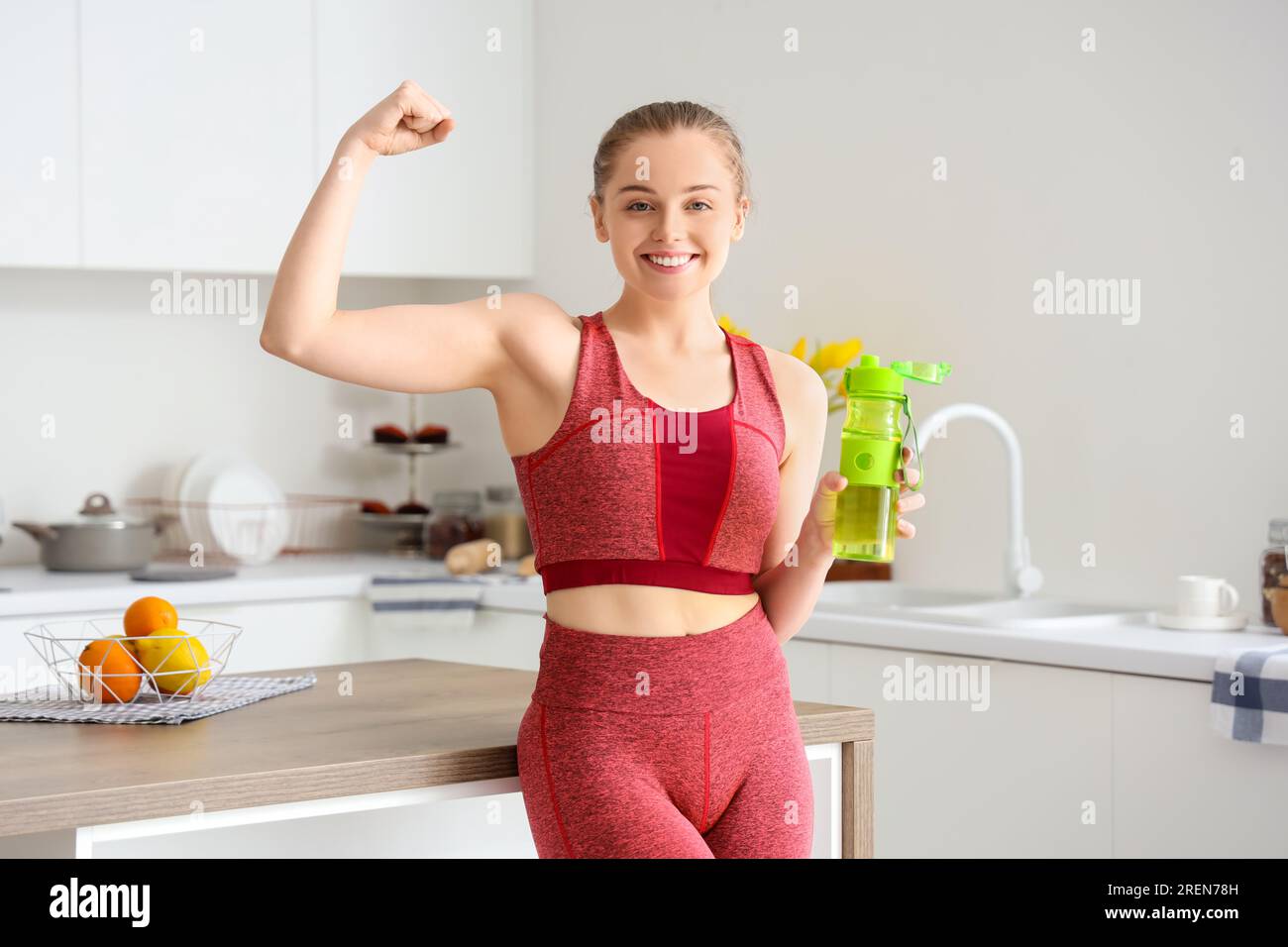 Sporty young woman with bottle of water flexing her arm muscles in ...