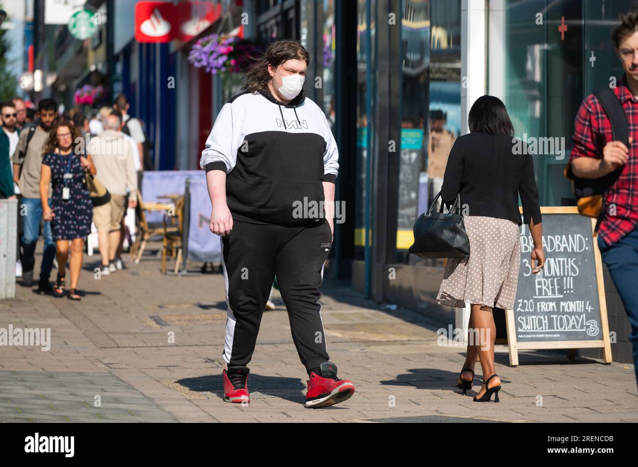 Overweight man walking in a busy urban shopping street in Summer, UK ...