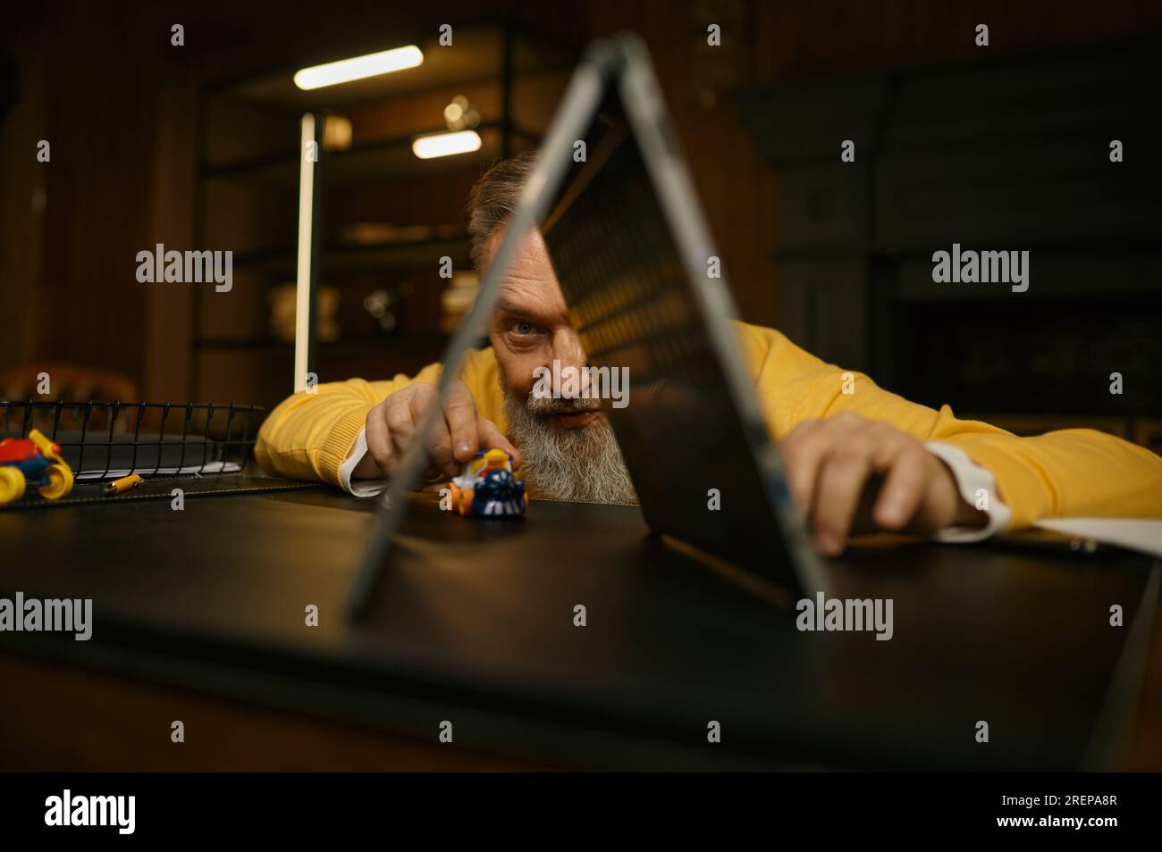 Senior man playing toys at workplace having fun after hard work in home ...
