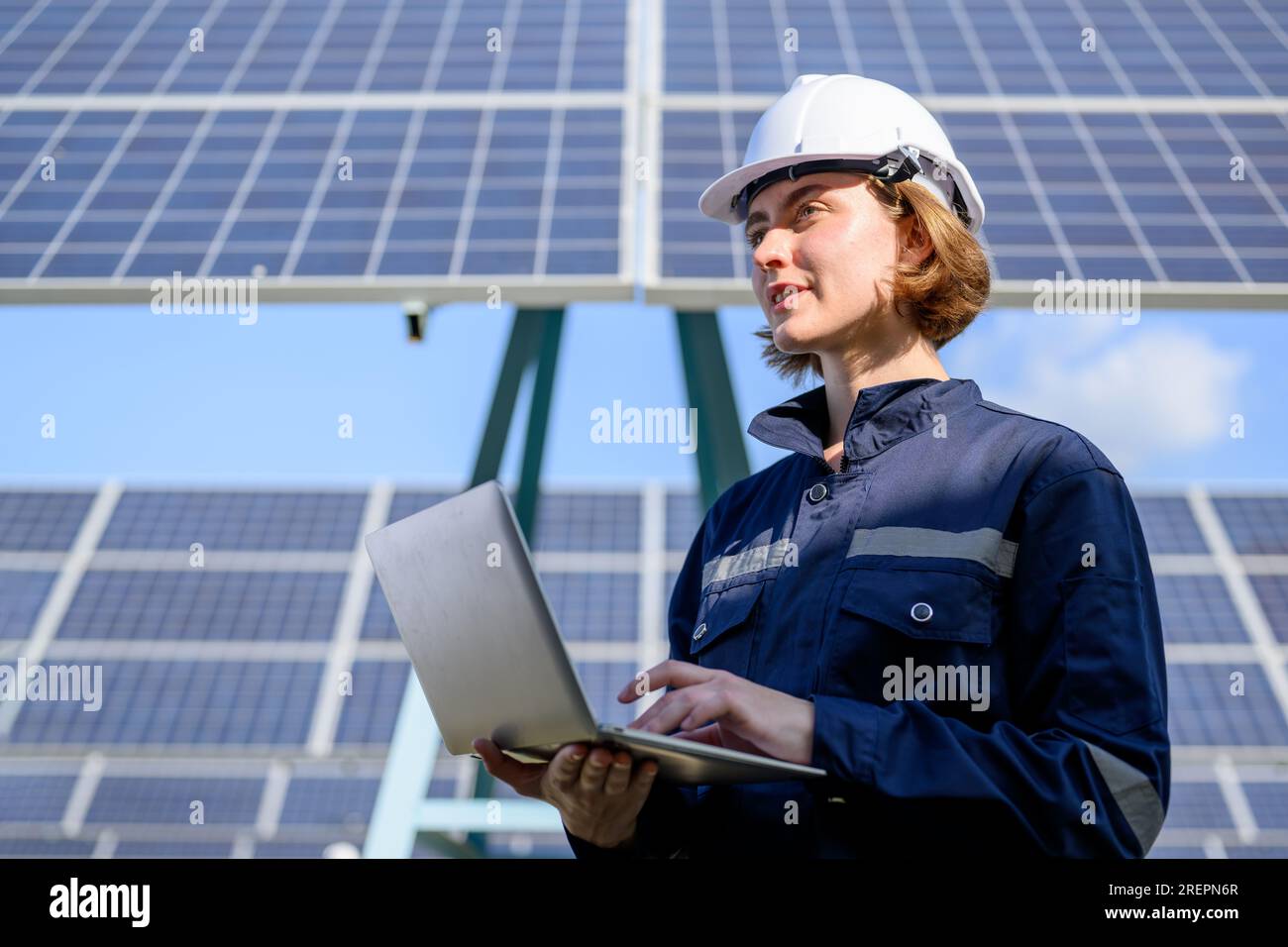 Female engineer holding laptop checking solar panels at solar farm ...