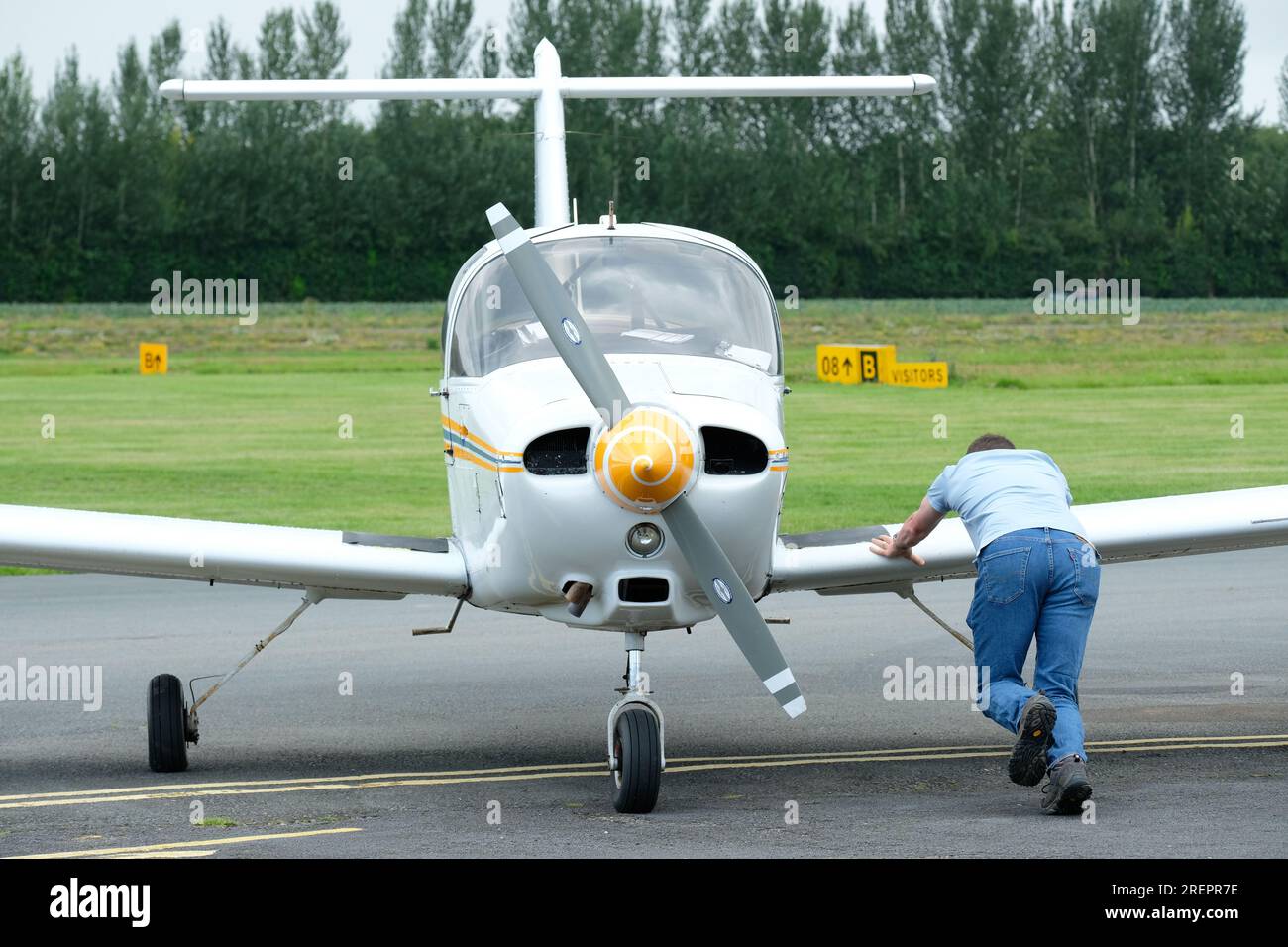 Pilot pushing a Piper Pa-38 Tomahawk light aircraft at a small general ...
