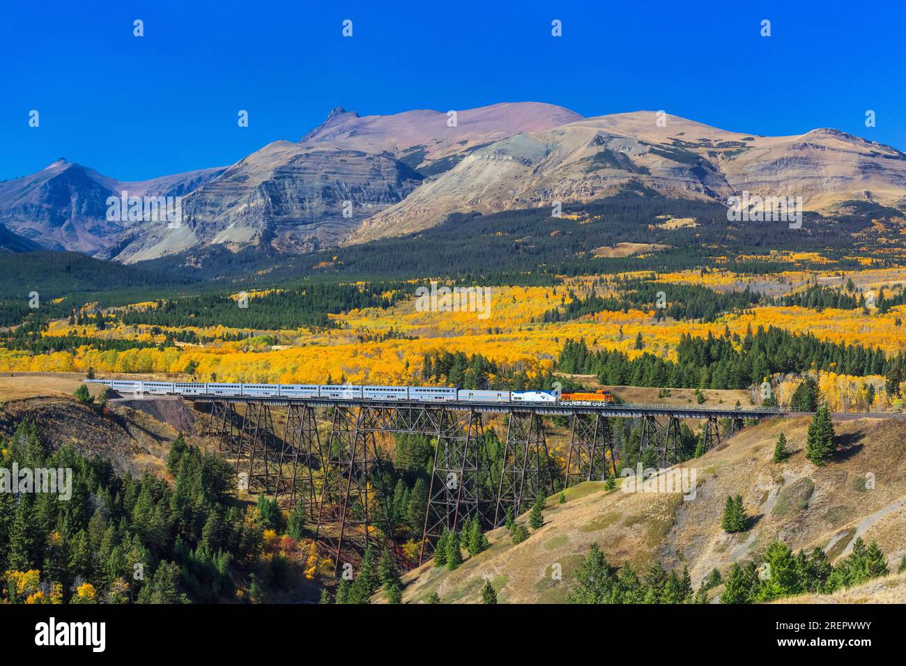 passenger train crossing over trestle in autumn below peaks of glacier ...