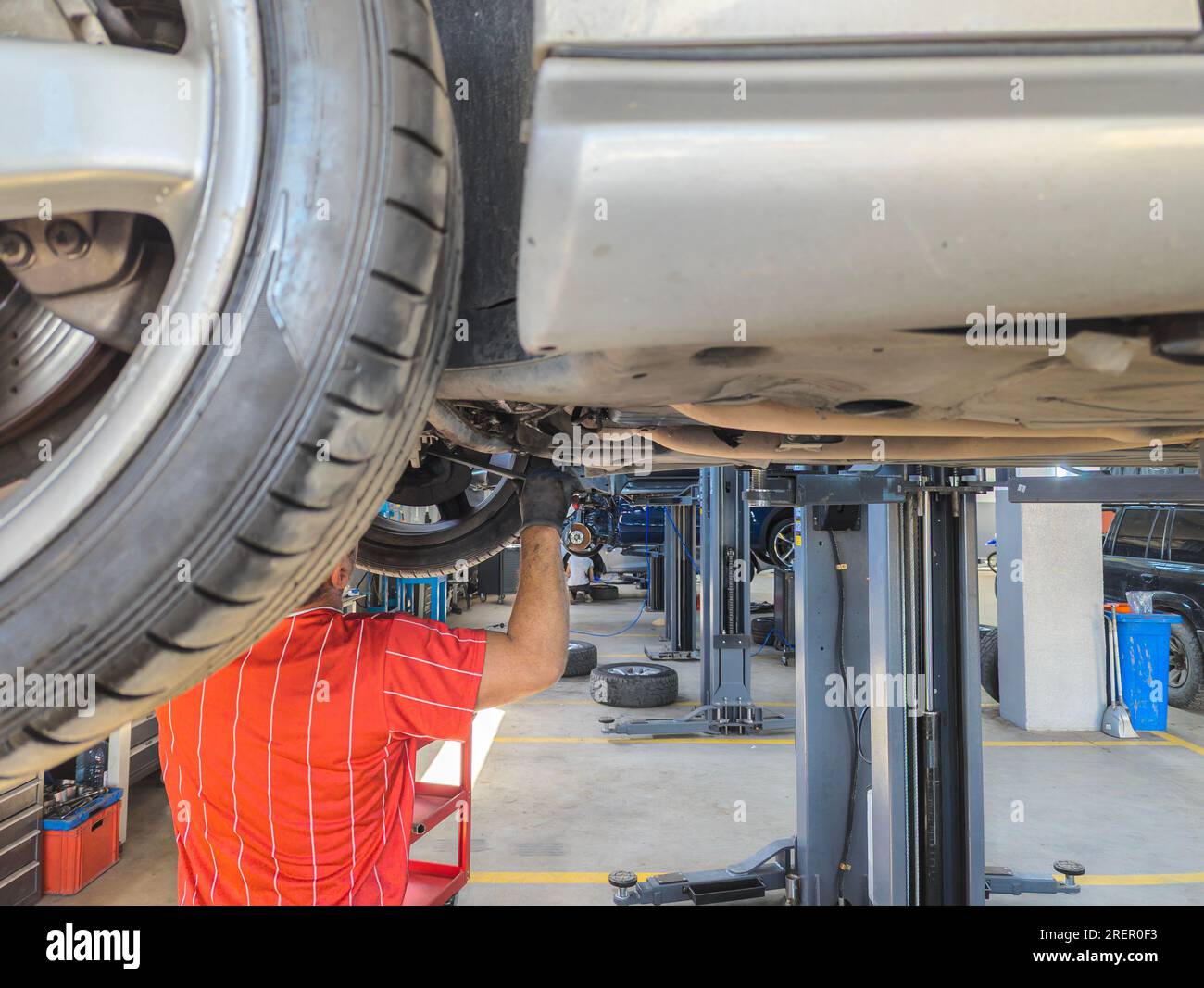 Technician inspecting car lifted in service center for maintenance ...