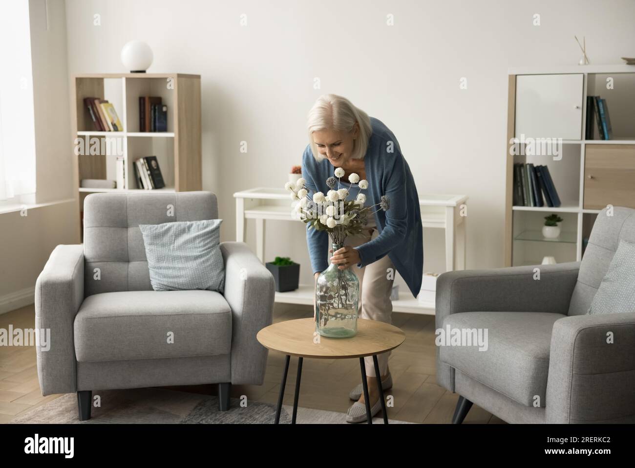 Happy blonde retired mature woman decorating home living room interior ...