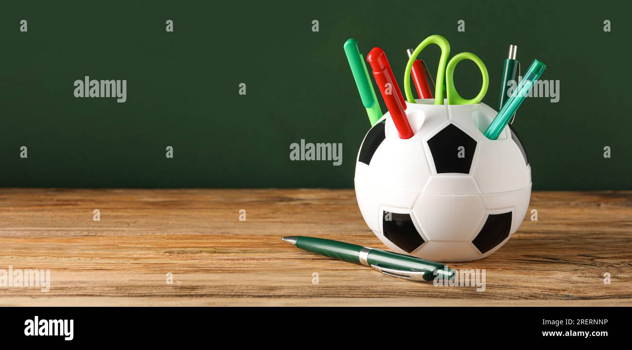 Stylish holder with school stationery on wooden table in classroom ...