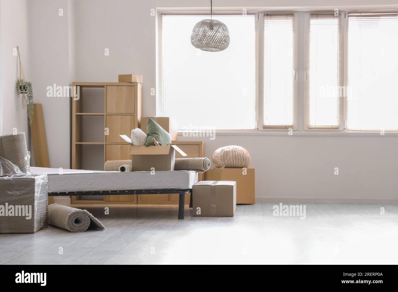 Bed with cardboard box and rolled carpet in room on moving day Stock ...