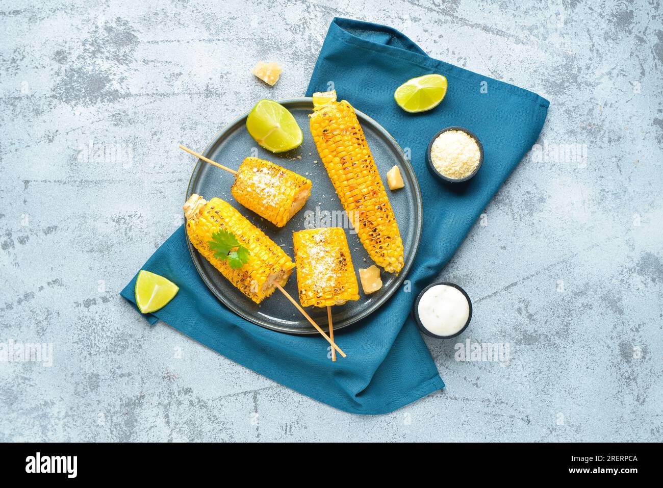 Plate with tasty grilled corn cob skewers and cheese on blue background ...