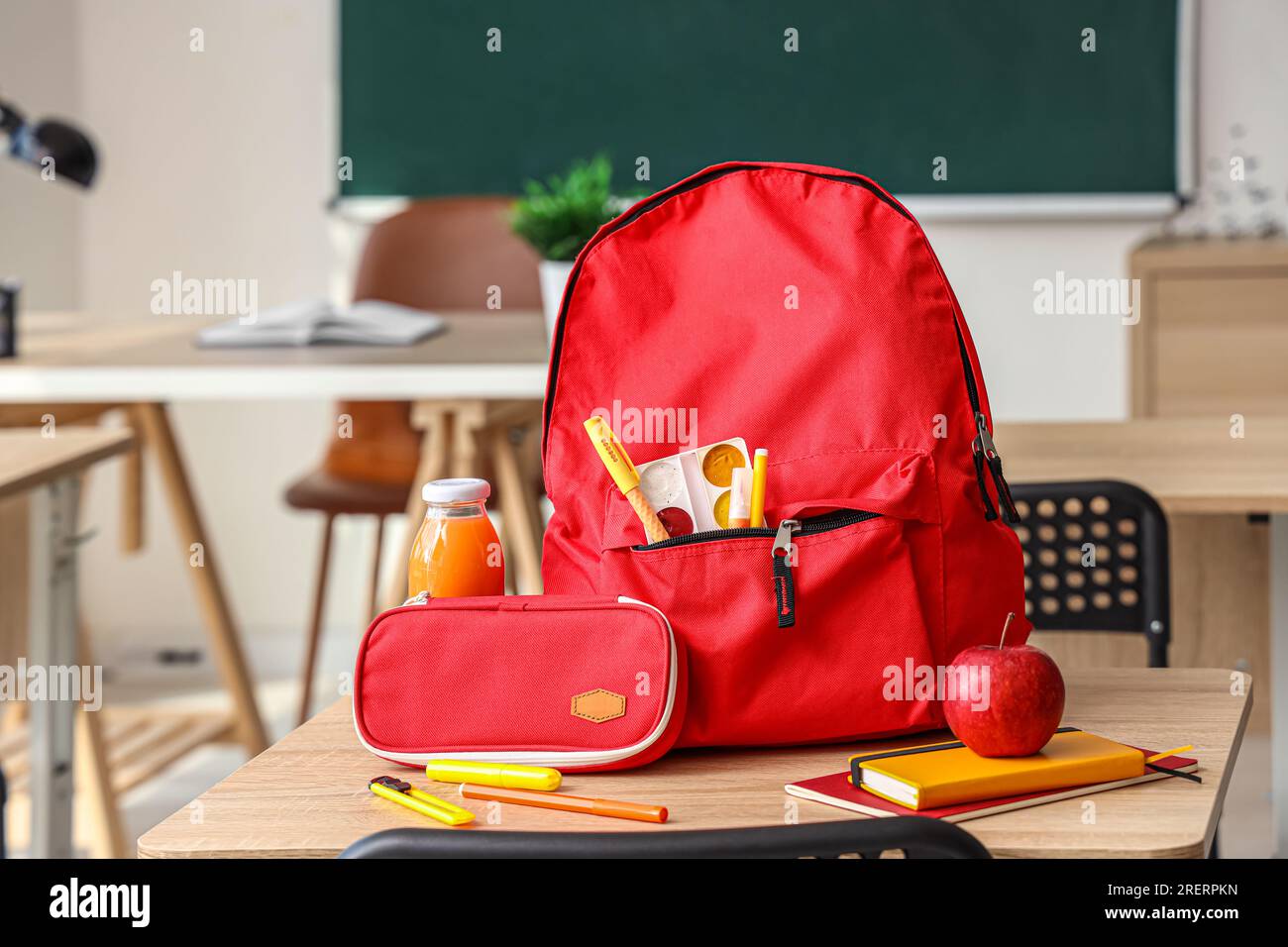 Red school backpack with stationery and lunch on desk in classroom ...