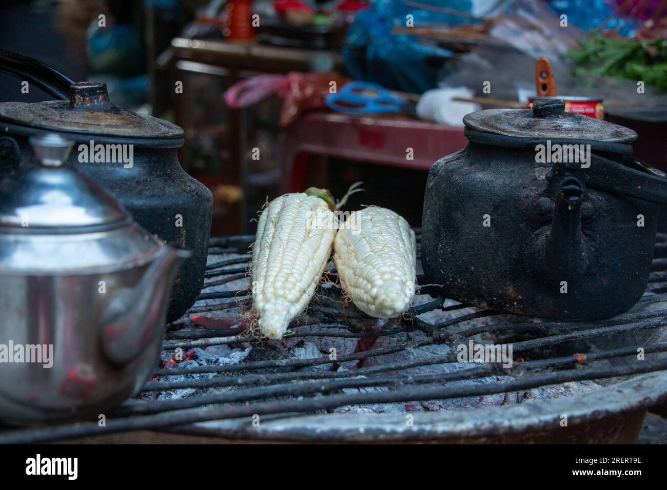 Corn cobs and tea kettles being heated on charcoal grill at a market in ...