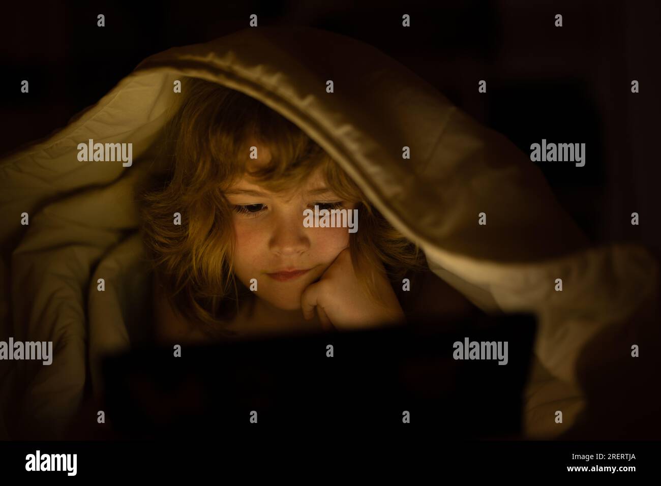 Kid alone at home. Kid boy lying on bed and surfing Internet on tablet ...