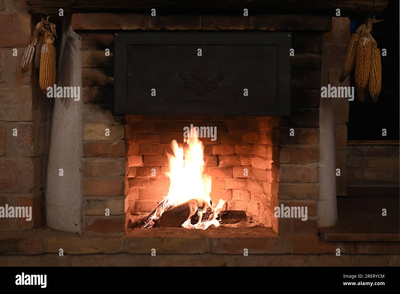 Rustic brick fireplace with burning fire and hanging dry corn cobs ...