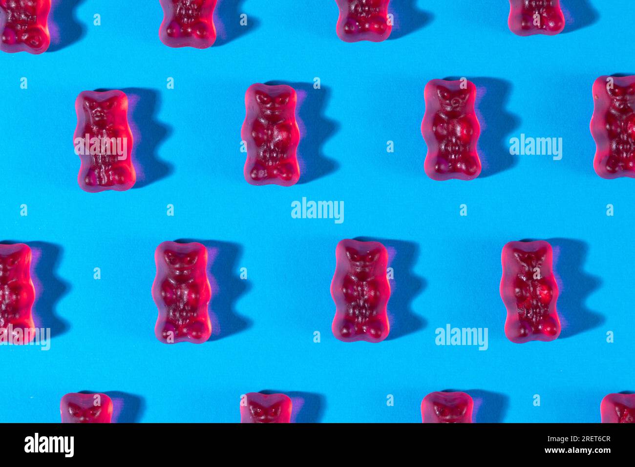 Red gummy bears in rows, on a blue background Stock Photo - Alamy
