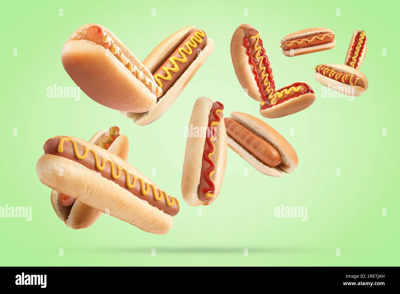 Many tasty hot dogs falling on light green background Stock Photo - Alamy