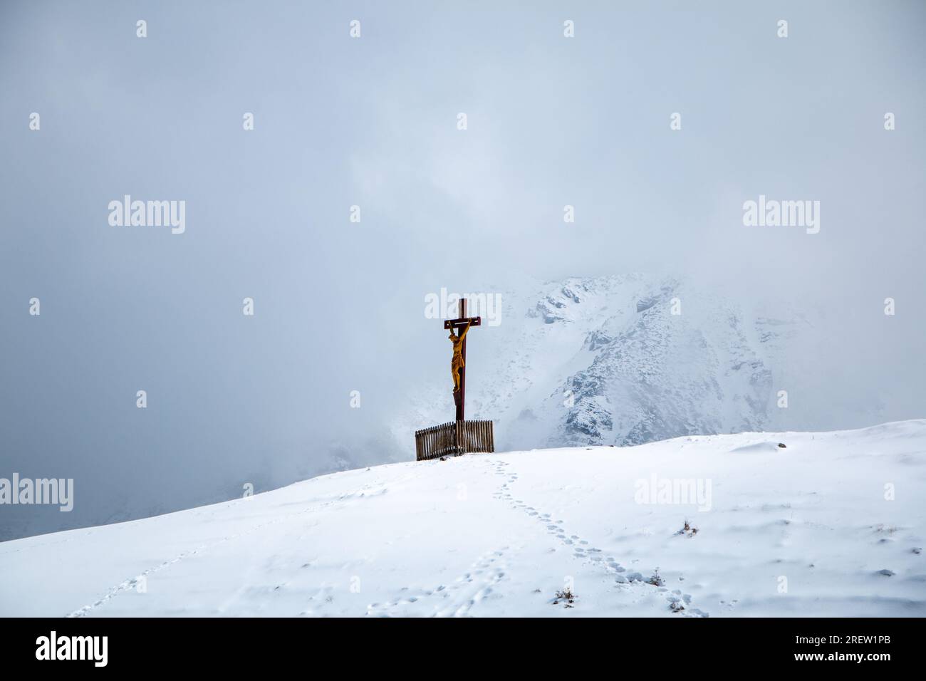 Footsteps in the snow leading to a statue of Jesus on the cross on top ...