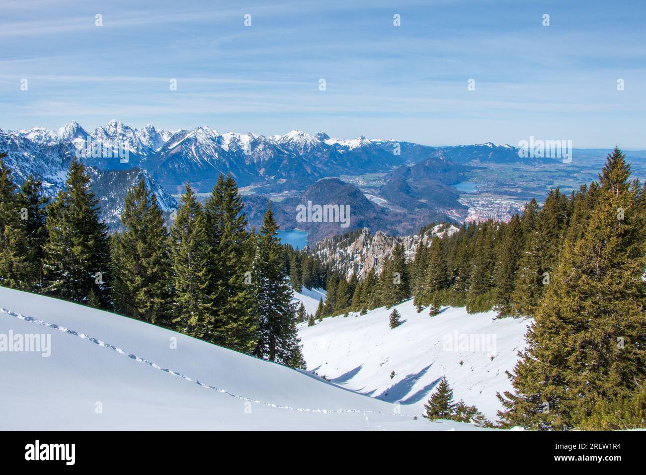 View across fields of thick snow towards Lake Alpsee, the town of ...