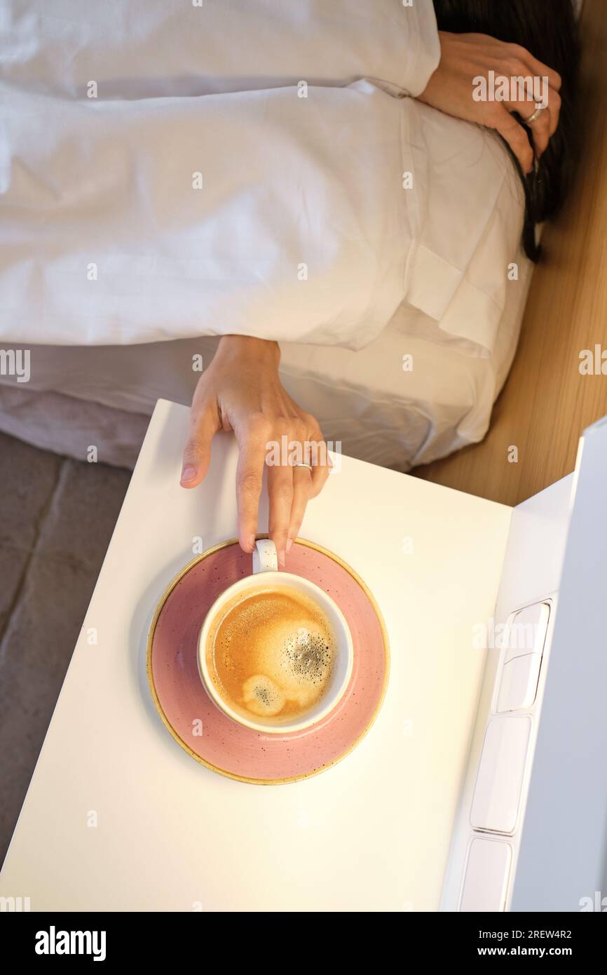 From above of awake crop woman lying in bed and hiding face under duvet ...