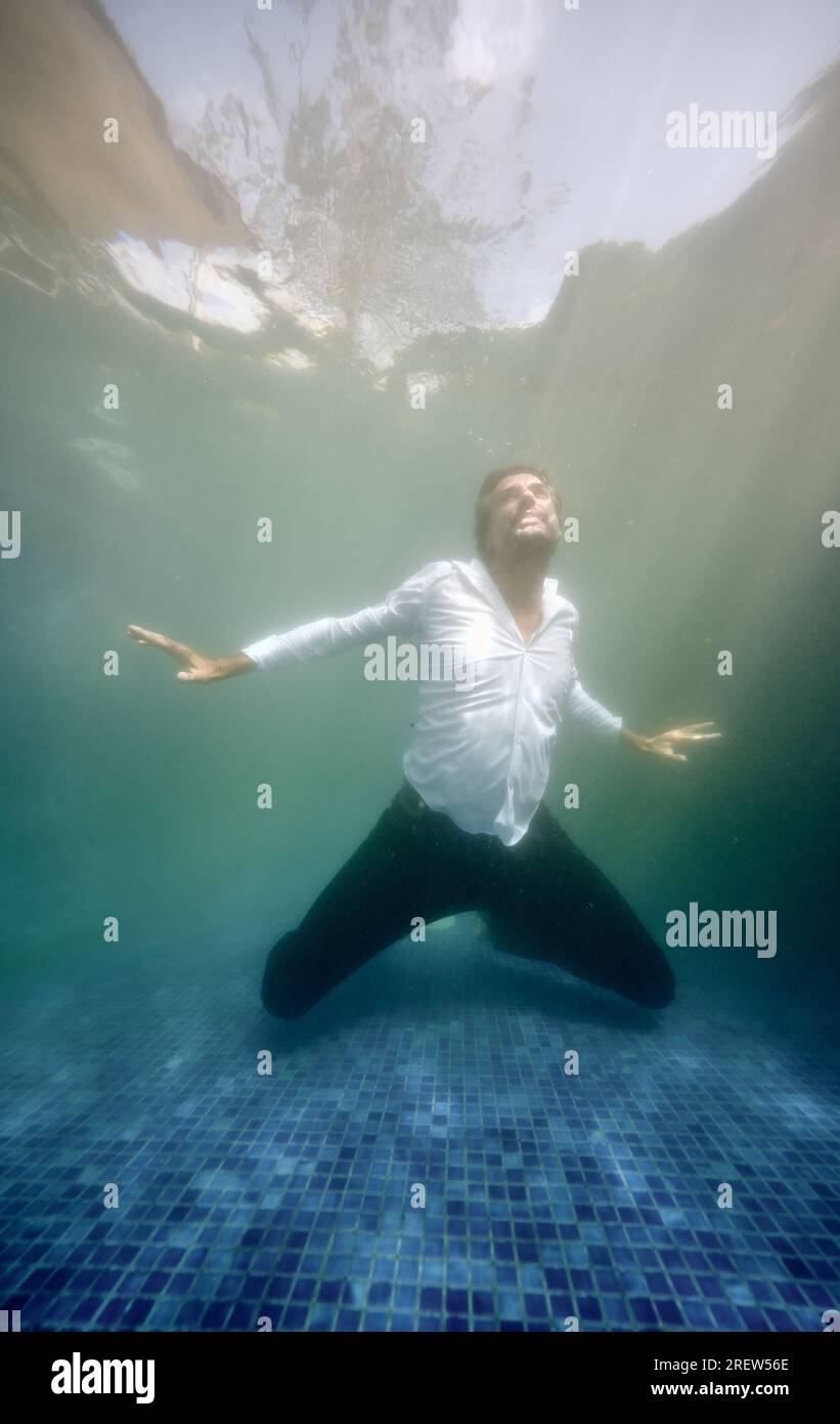 Underwater view of mature male in clothes drowning in swimming pool ...
