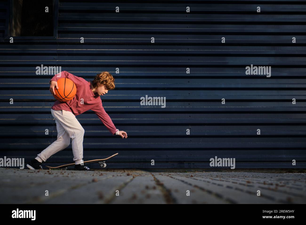 Full body boy with basketball ball bending near skateboard while ...
