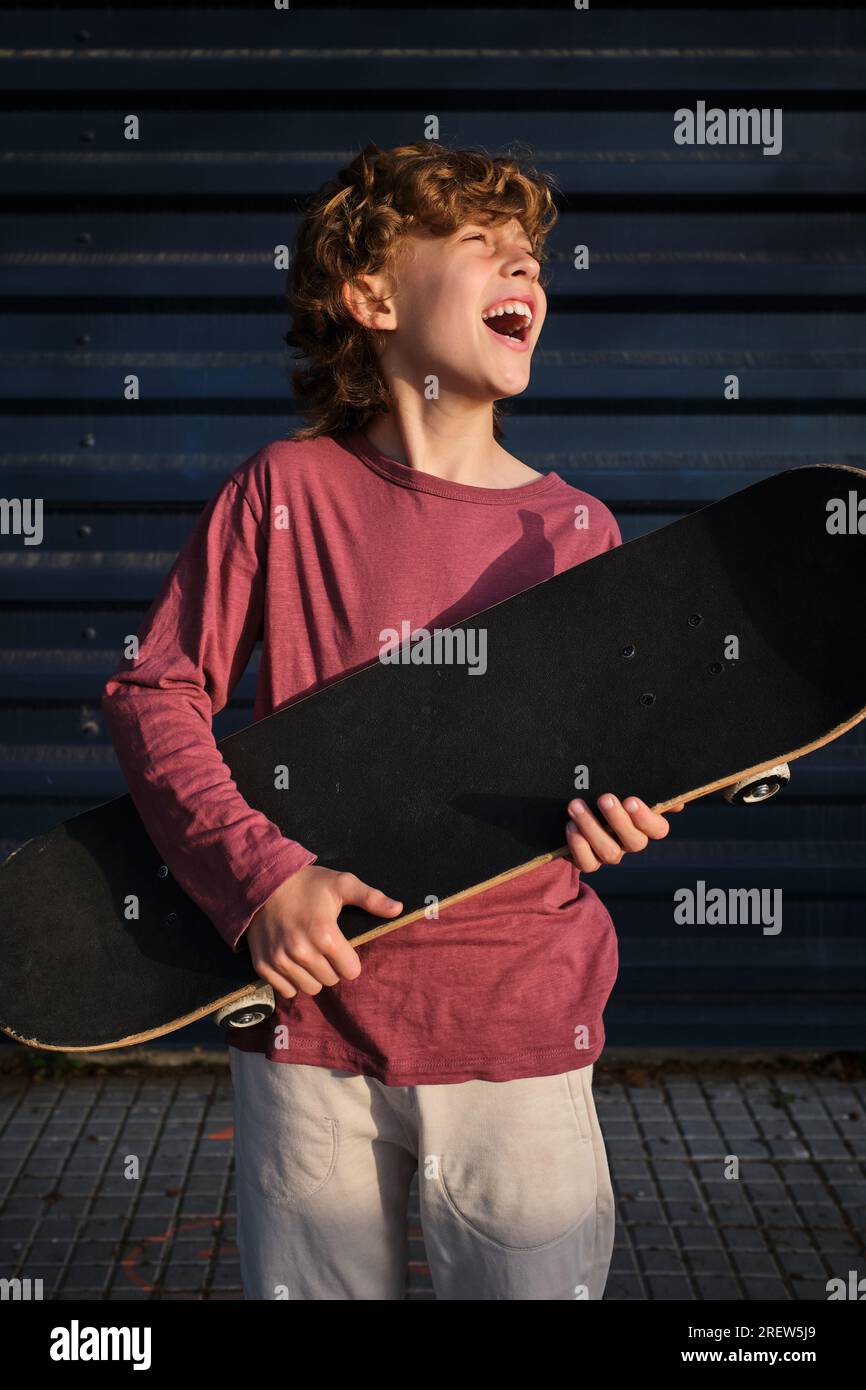 Happy little skater with skateboard laughing and looking away while ...