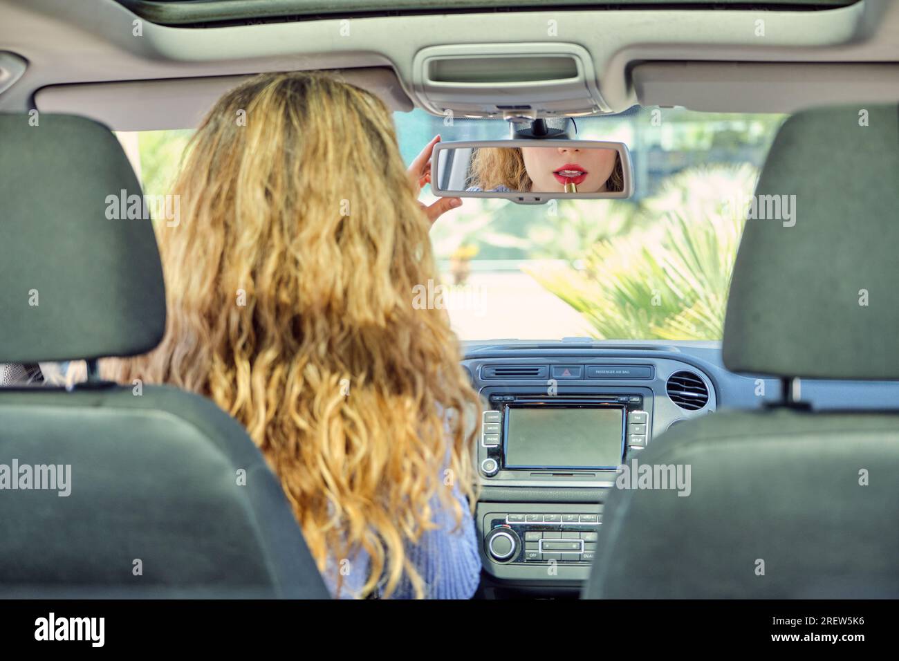 Back view young female driver applying red lipstick against vanity ...
