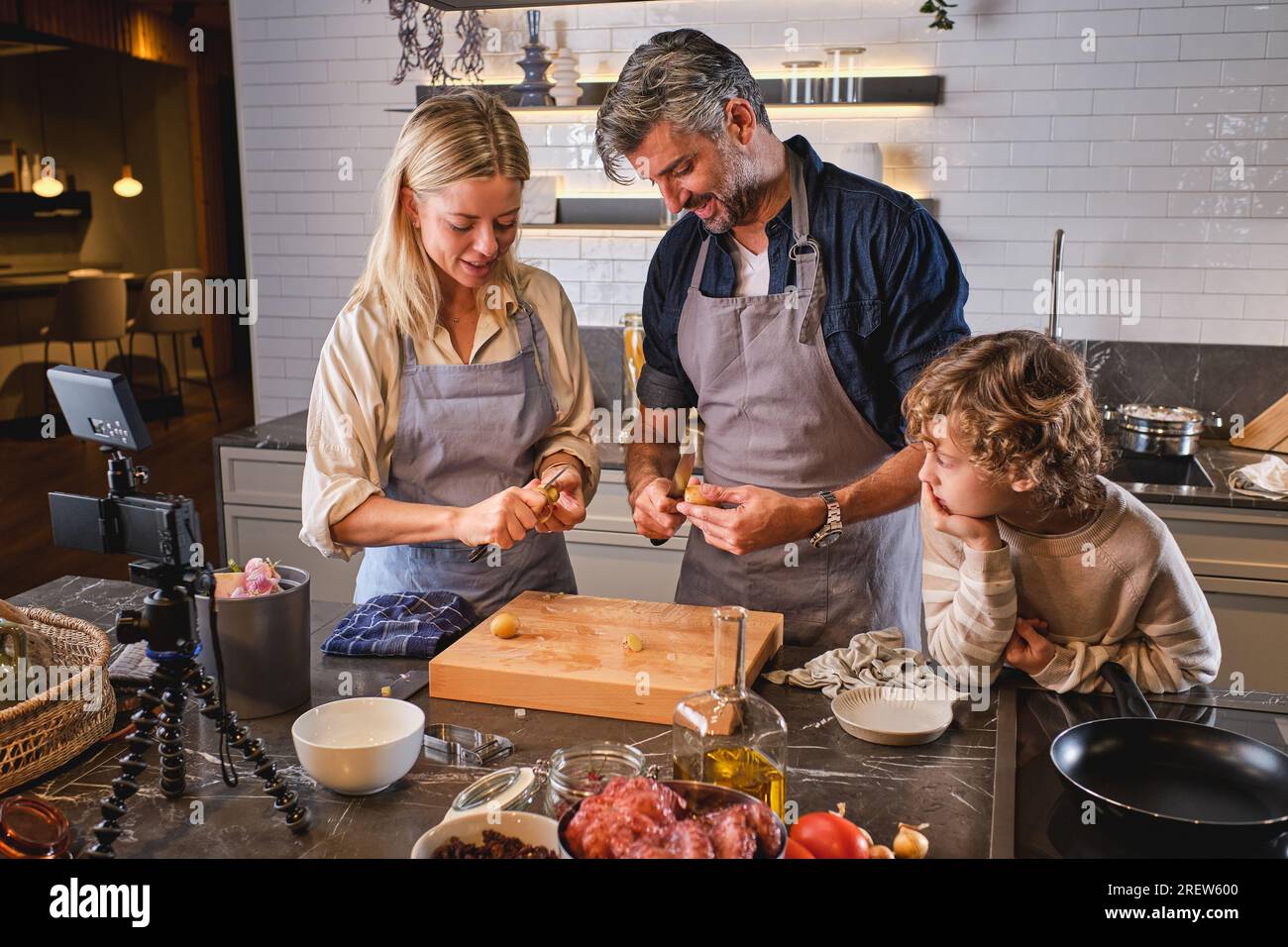Cute kid looking at parents peeling raw potatoes at table and recording ...