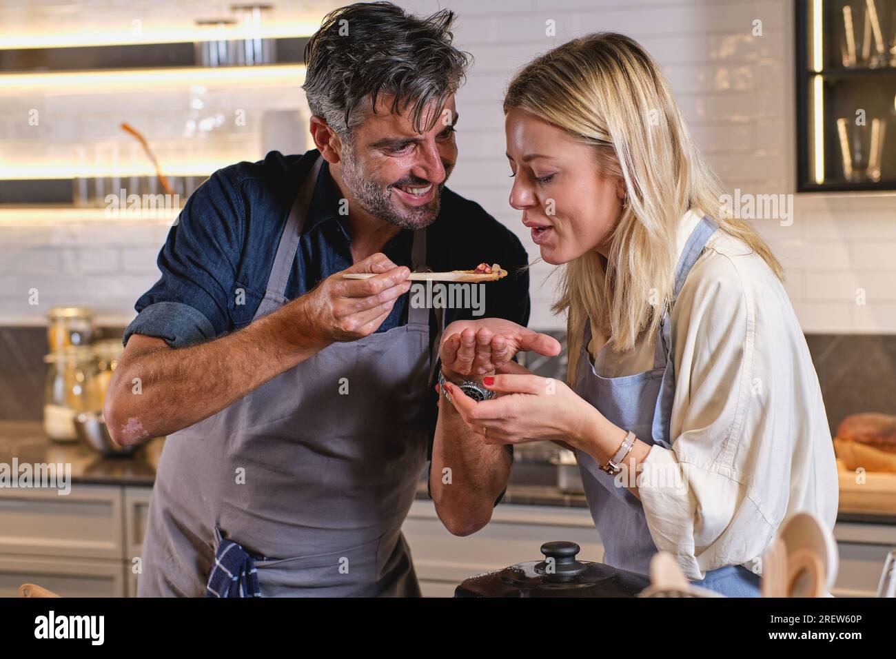 Loving couple having fun while cooking together and tasting dish in ...
