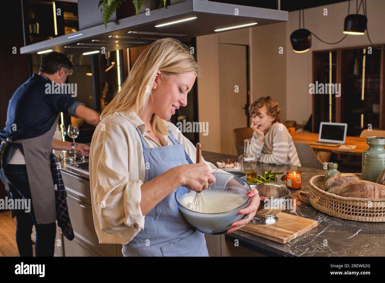Woman and man in aprons cooking together against boy sitting at counter ...