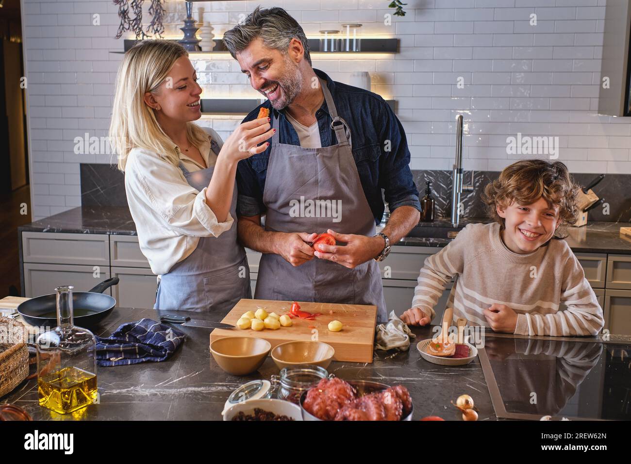 Positive woman giving husband slice of fish to taste while son standing ...