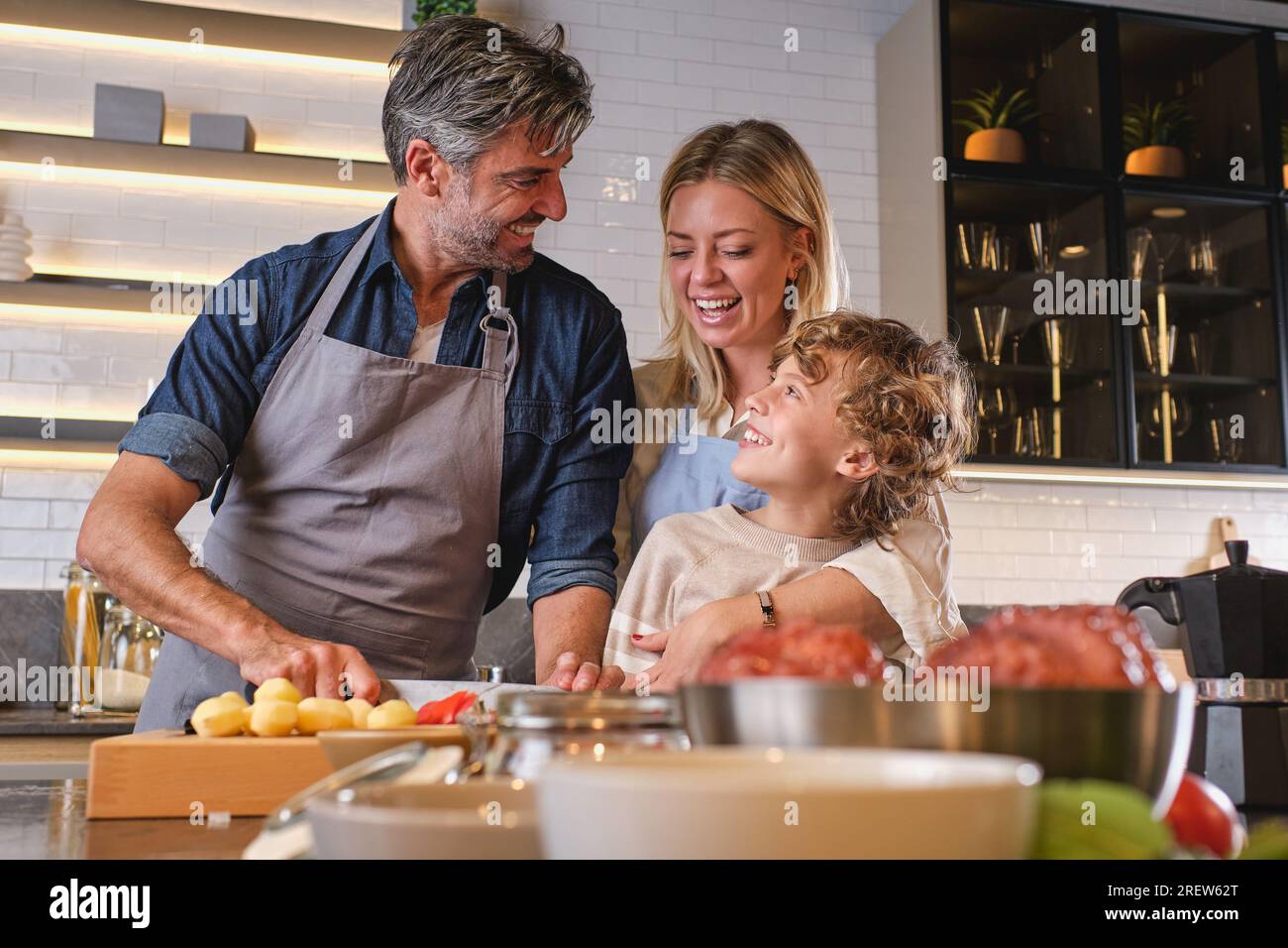 Laughing adult man in blue shirt showing son how to cook while woman ...