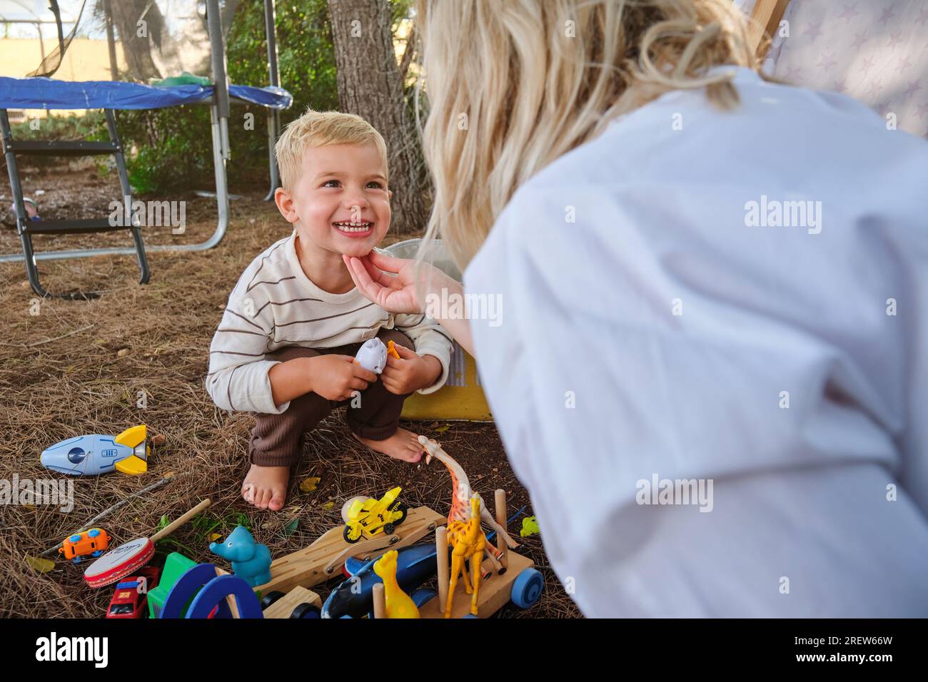 Crop mother tickling chin of adorable boy sitting on haunches while ...