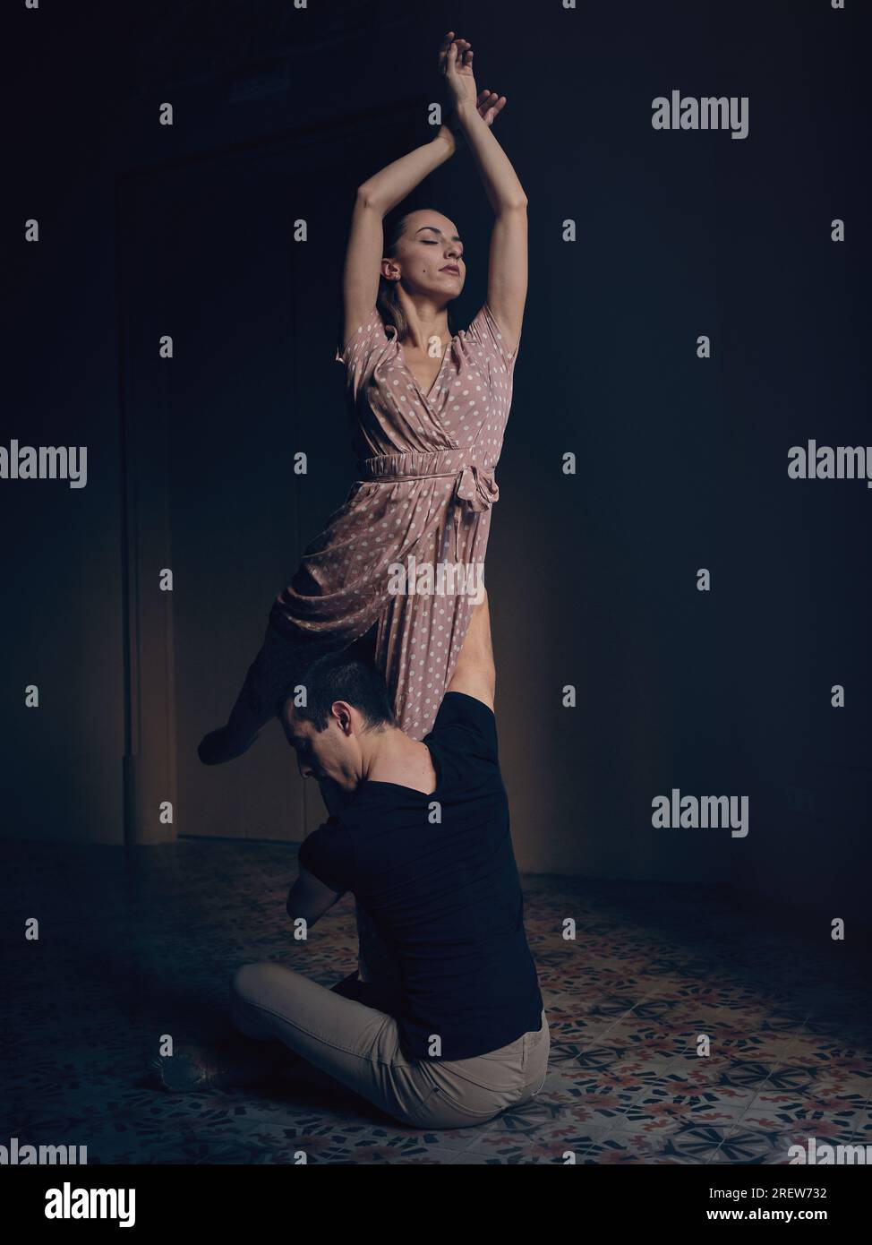 Full body of man sitting on floor and raising female dancer in pose ...