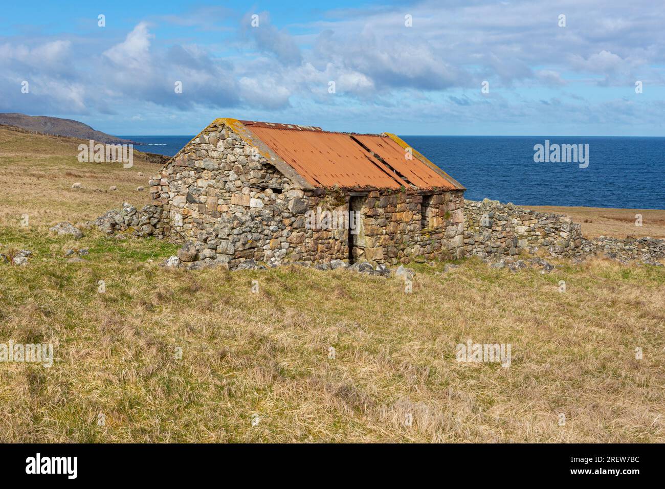 A small stone building with a rusty metal roof by a calm blue sea on ...