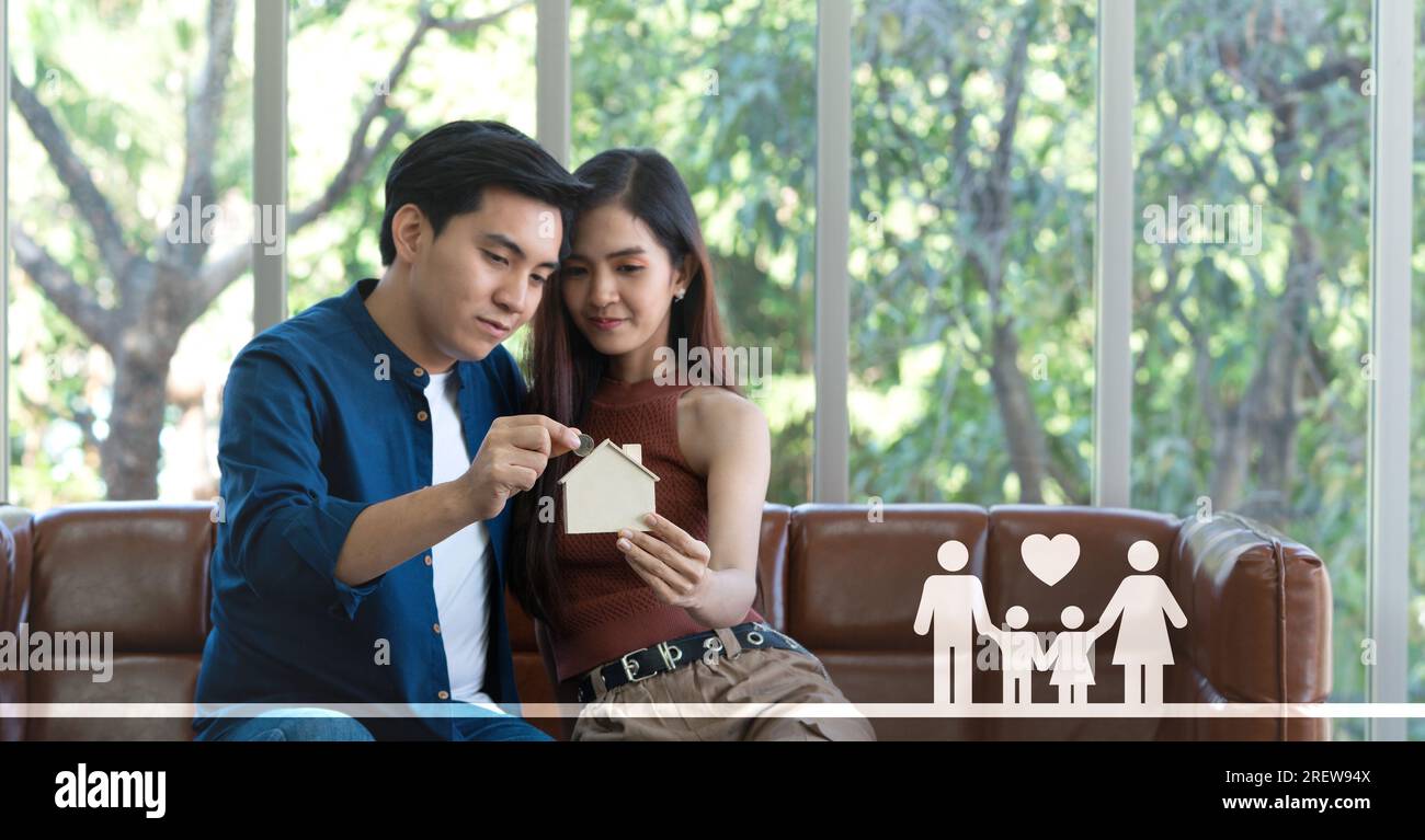 Young asian couple sits on a cozy couch, putting silver coin into a ...