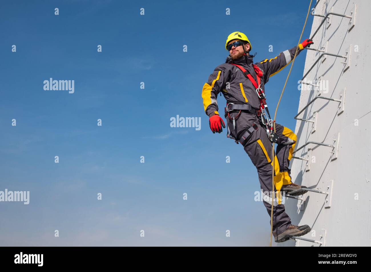 Industrial climber, a worker in a helmet and a safety belt, holds on to ...