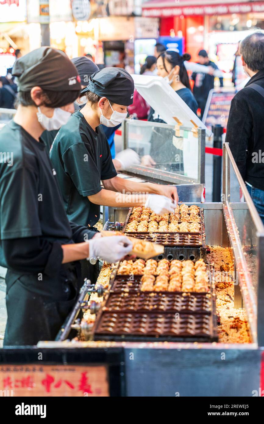 Side view of three cooks in line preparing and cooking takoyaki ...