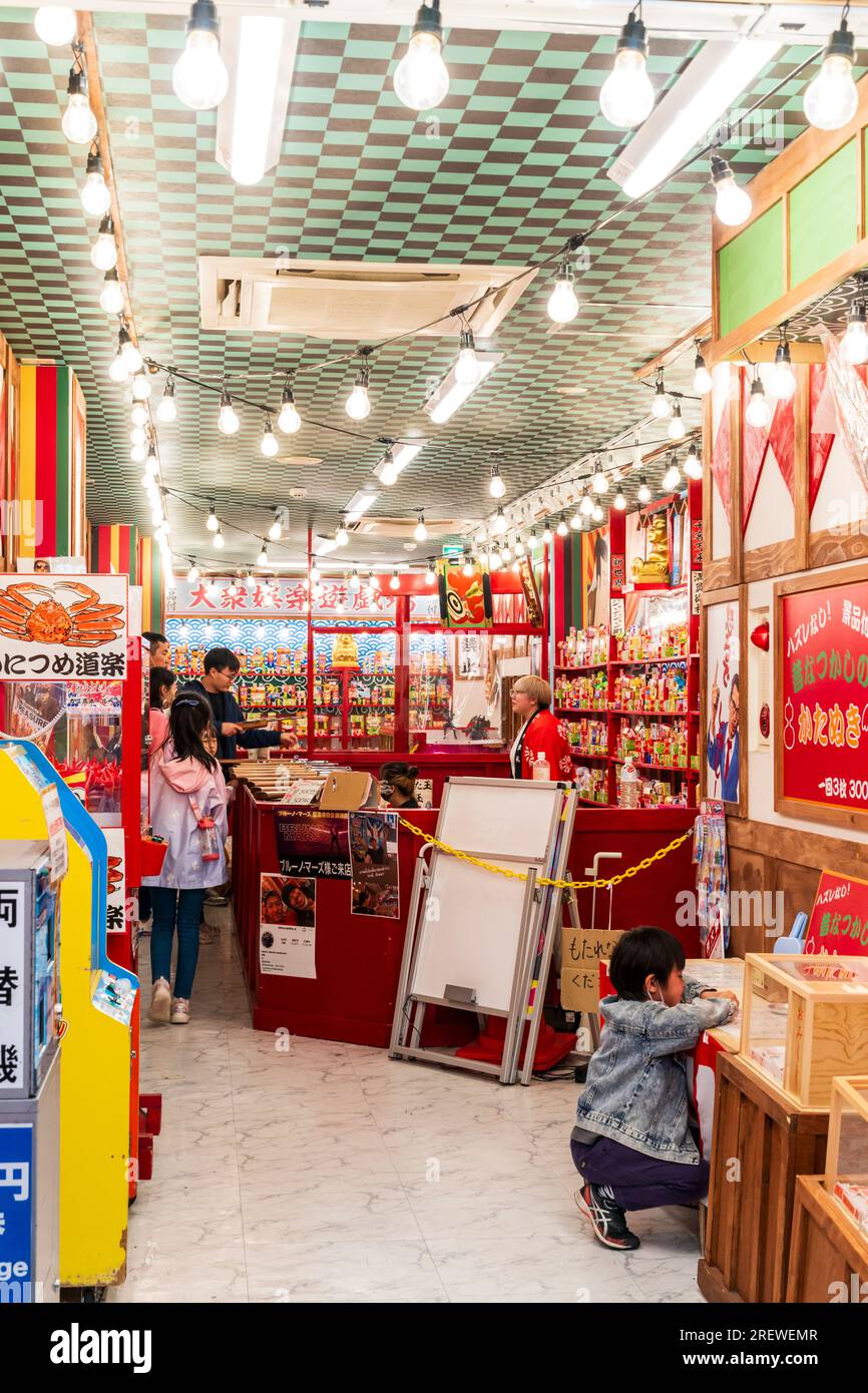 View along the brightly lit interior of a shooting gallery in Dotonbori ...