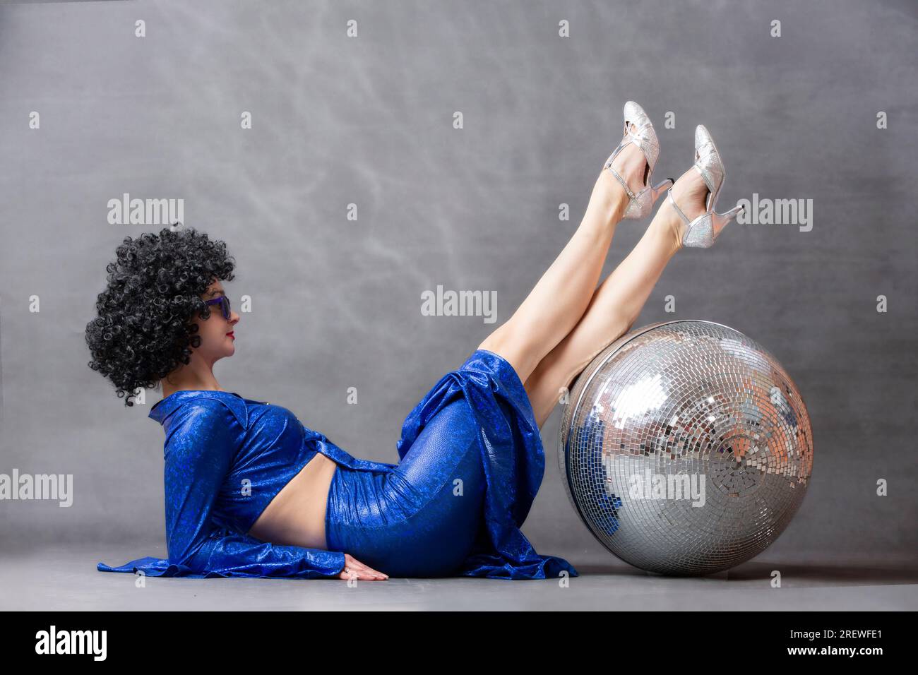 Girl with a disco ball in an afro wig on a gray background. Disco style ...