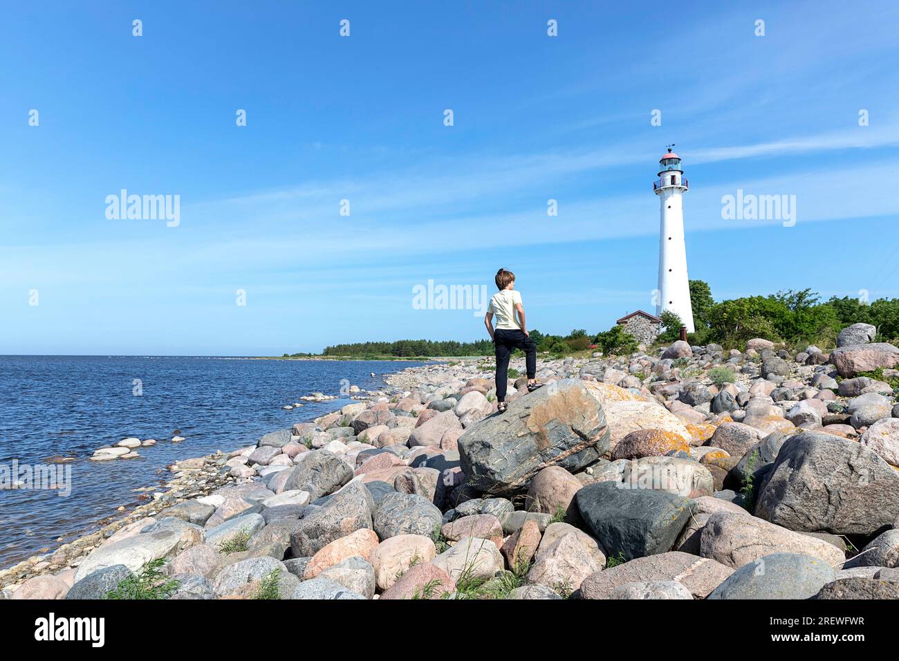 Boy tourist on spectacular stony beach with Kihnu lighthouse in the ...