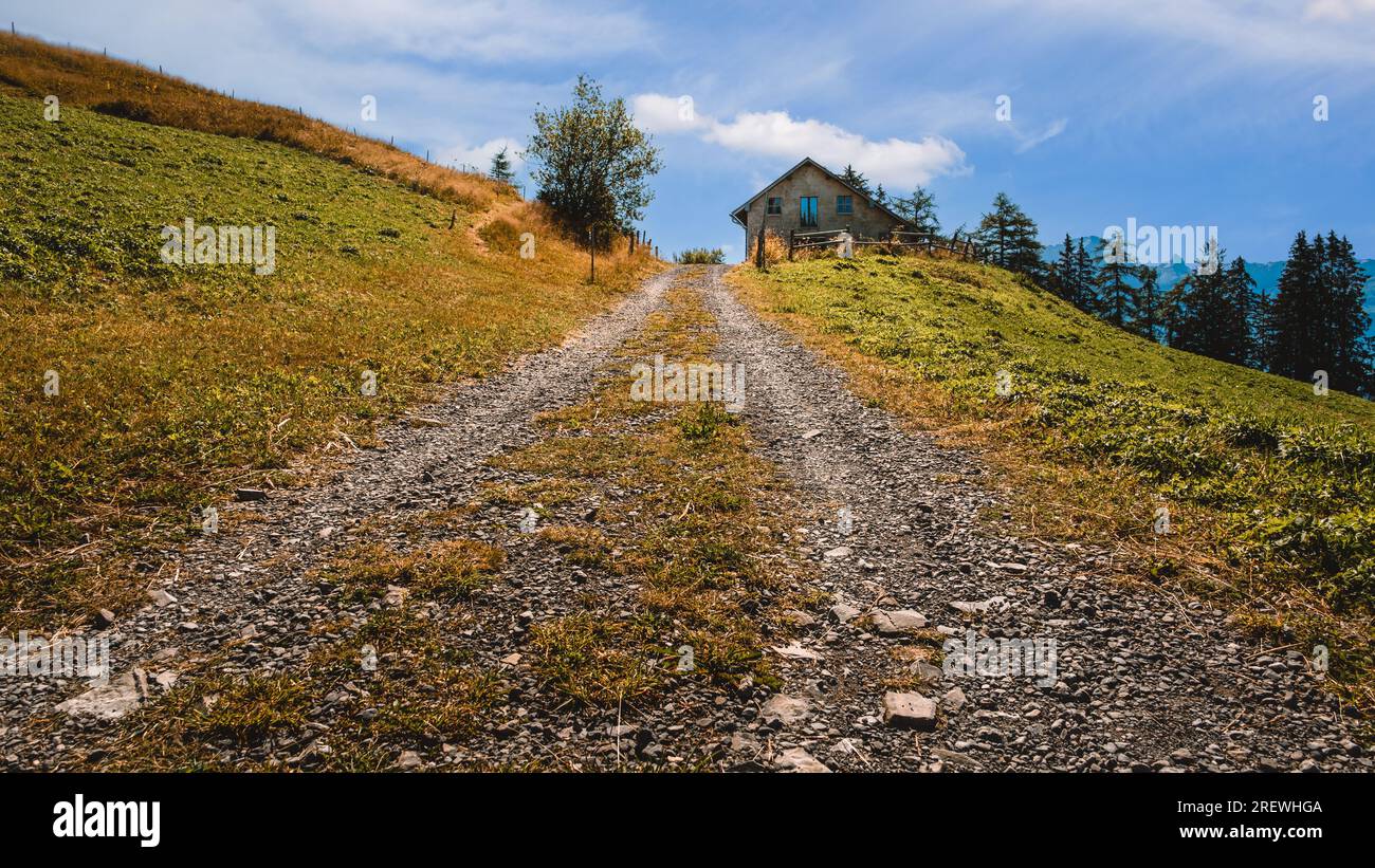 Gravel road leading uphill to a concrete cottage in between alpine ...