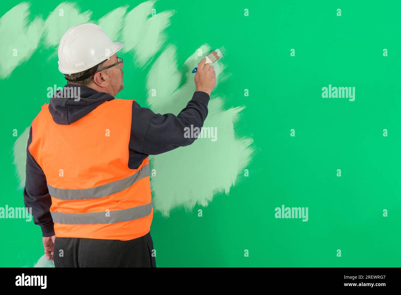 A painter in overalls and a helmet paints a wall with a brush. Copy ...