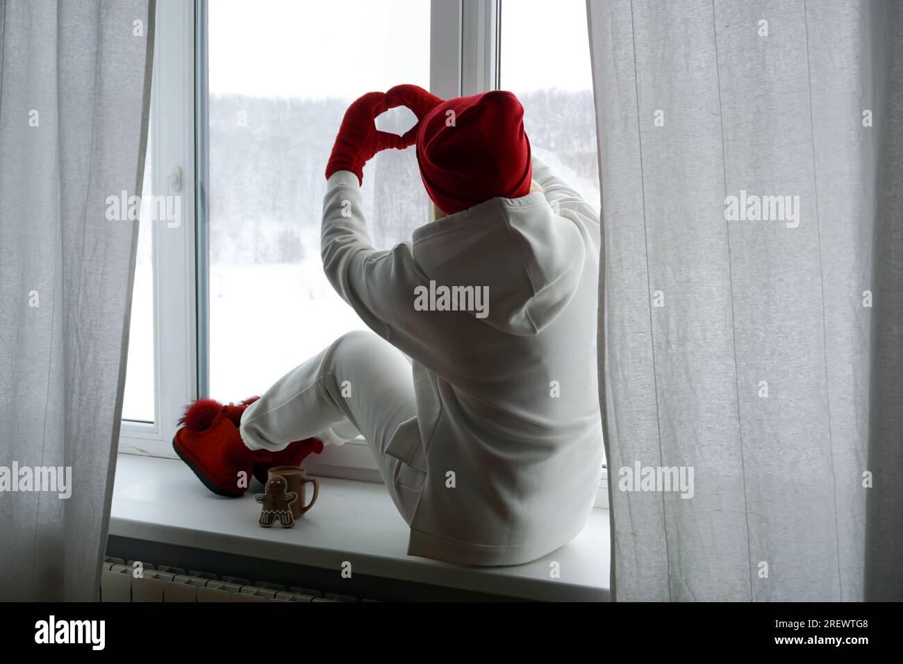 A woman in a white suit sits on the windowsill and looks out the winter ...