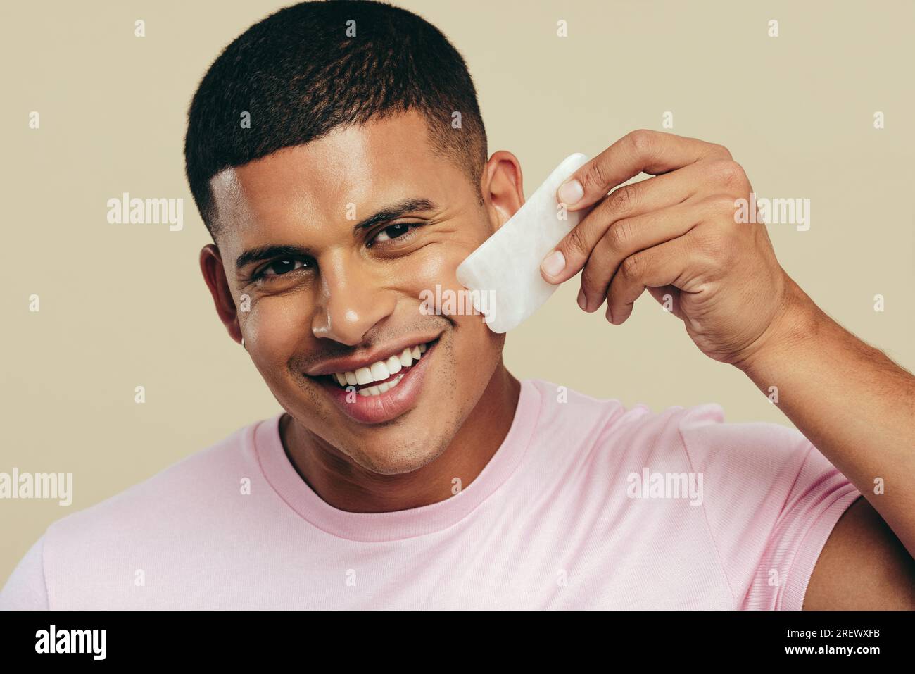 Happy young man improving his beauty with a gua sha massage on his face ...