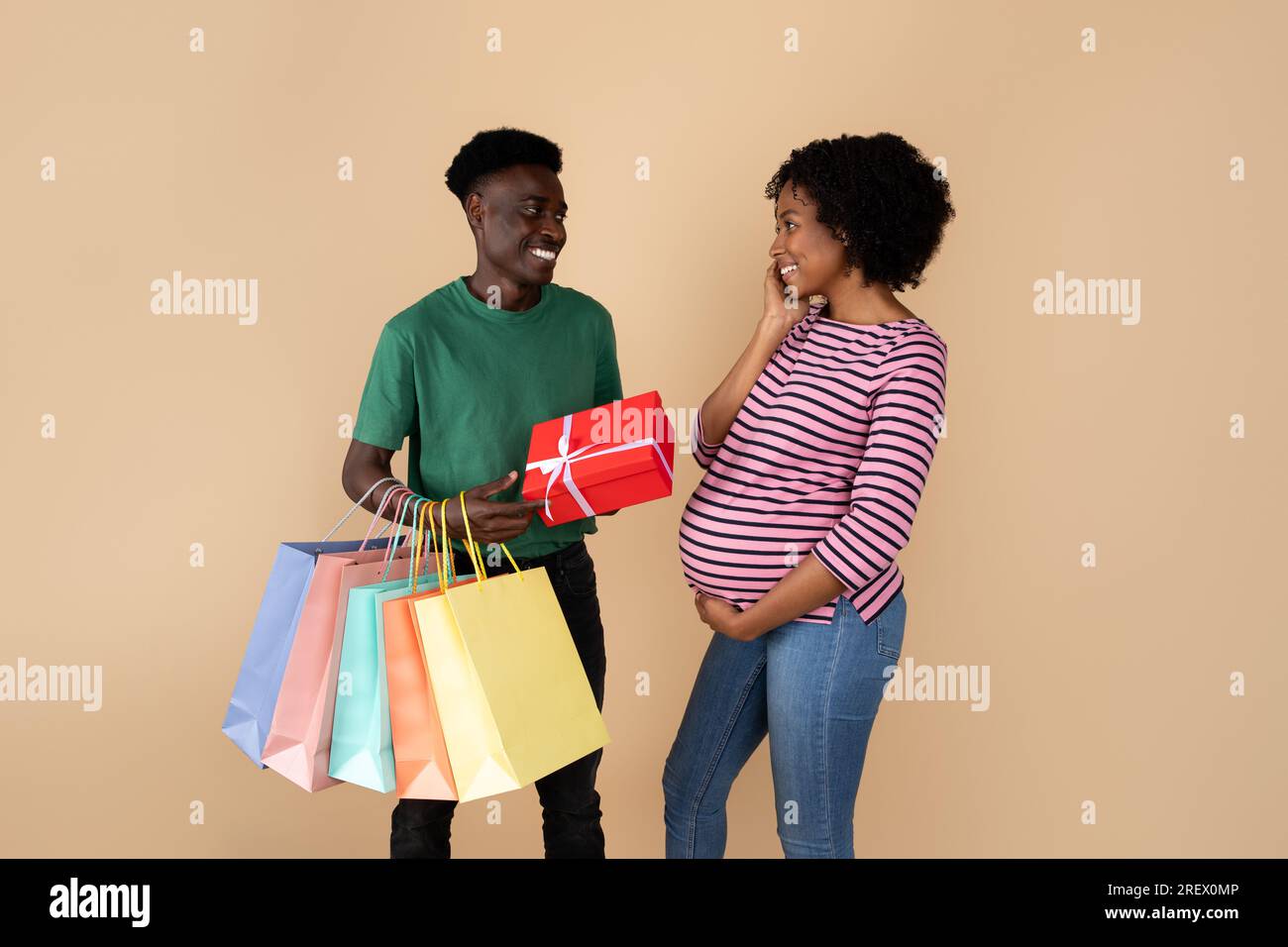 Happy young black man gives gift box to lady with belly with many ...