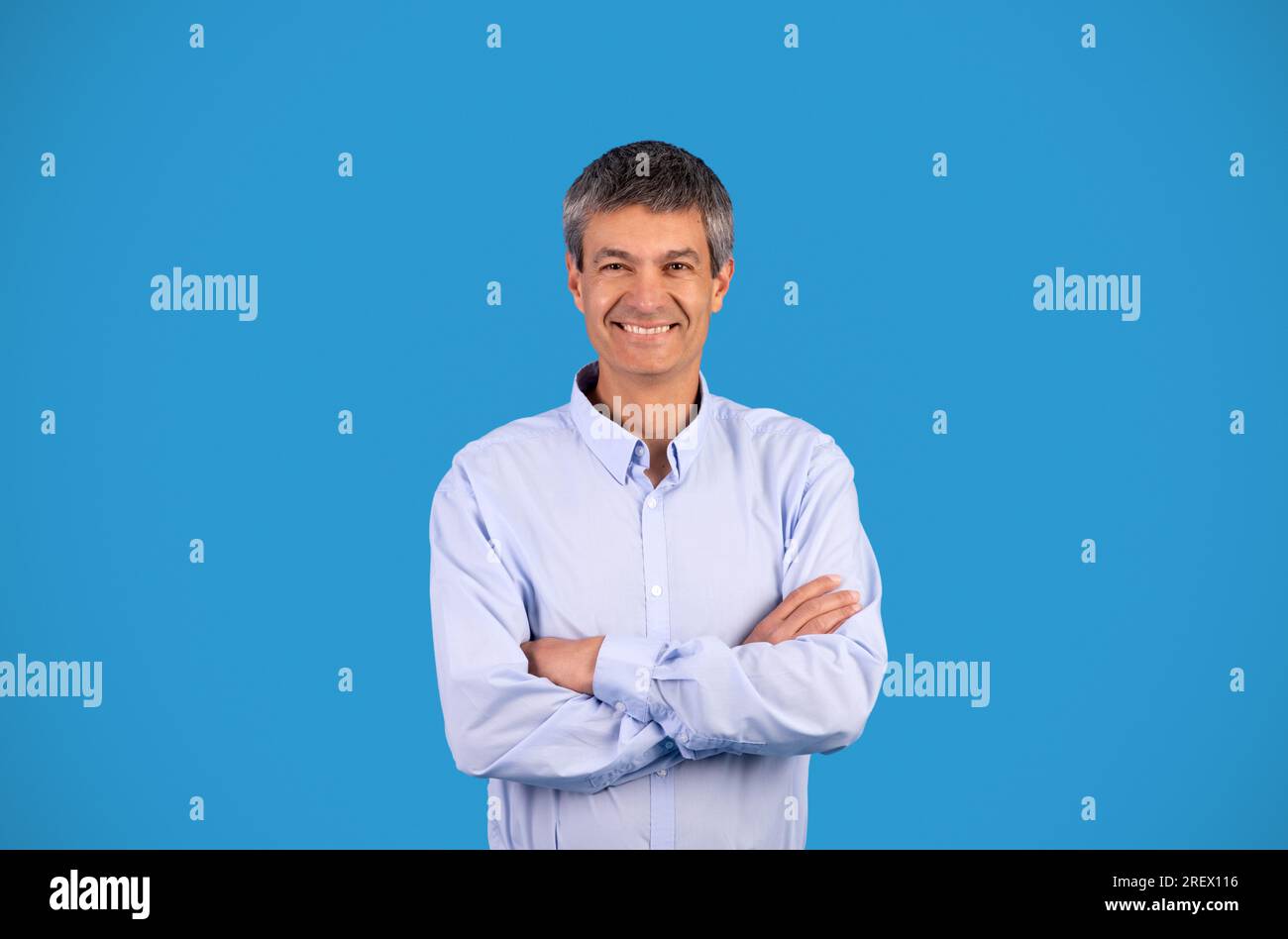 Portrait of confident mature businessman crossing hands over blue ...
