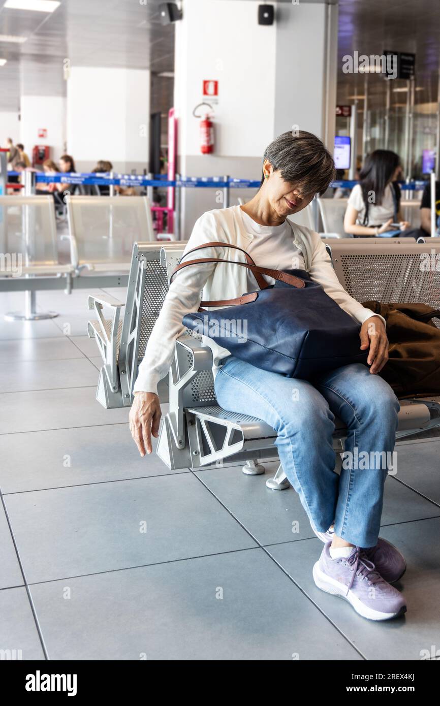 Tired Asian woman sleeping on airport departure waiting area chairs while waiting for flight ...