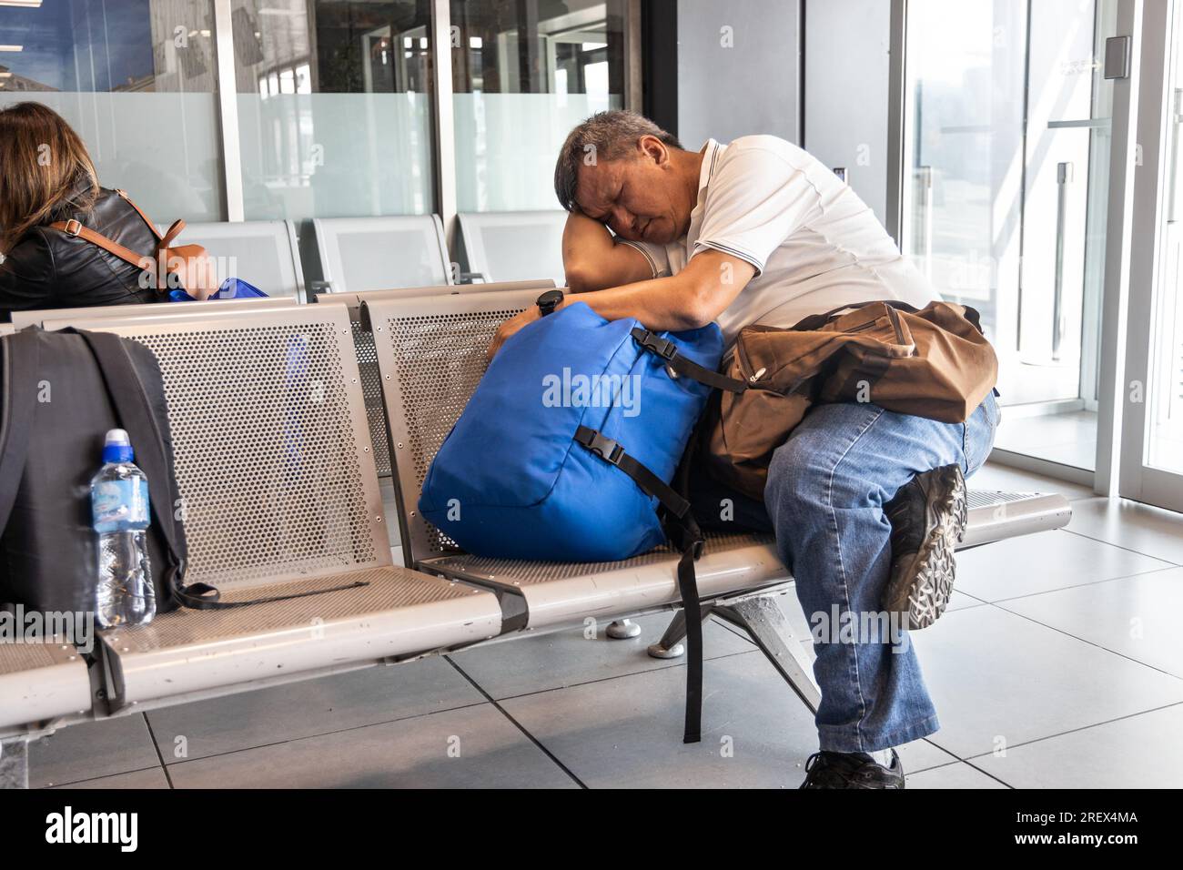 Tired Asian man sleeping on airport departure waiting area chairs while ...