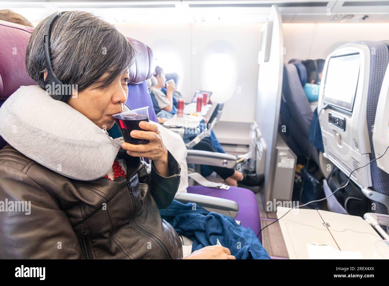 Asian woman drinking red wine whilst enjoying inflight entertainment ...