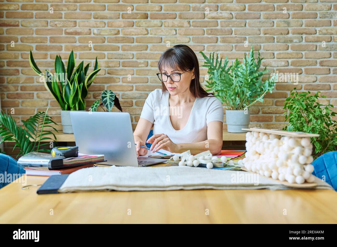 Mature woman interior designer working at her desk with fabric samples ...