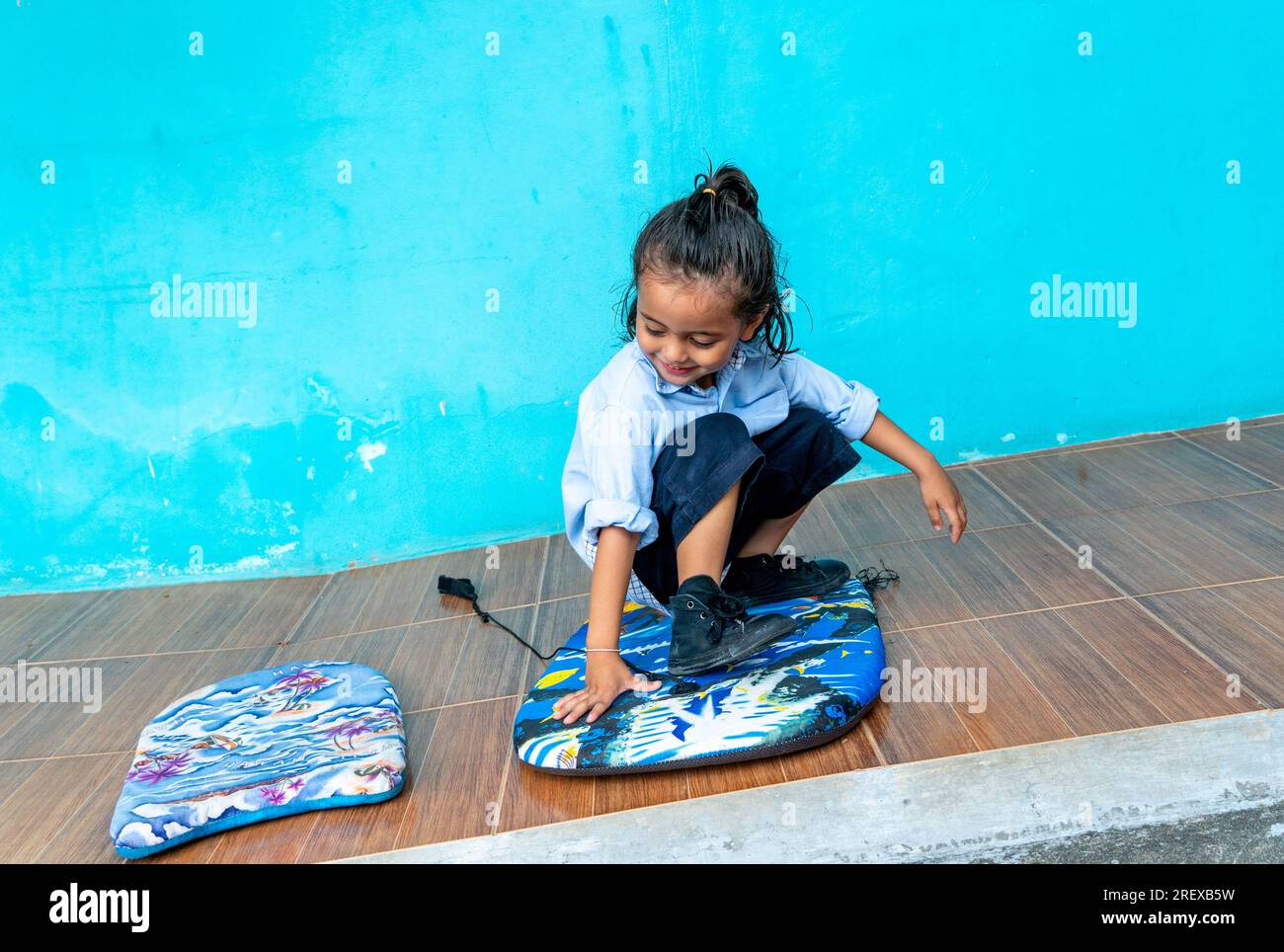 A cute boy with long hair practicing surfing in different poses at home ...